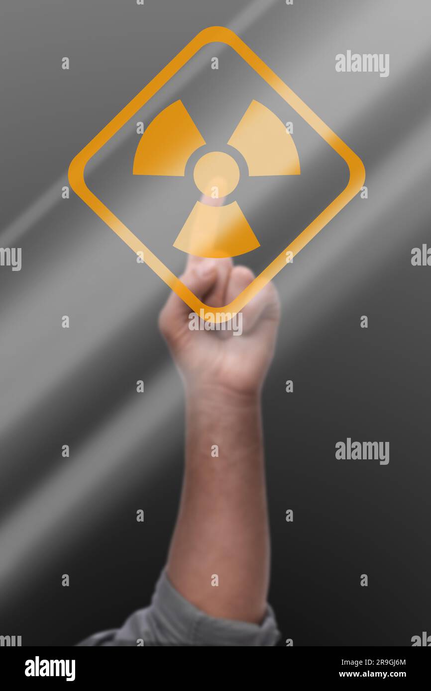 Man touching radiation warning symbol on digital screen against grey ...
