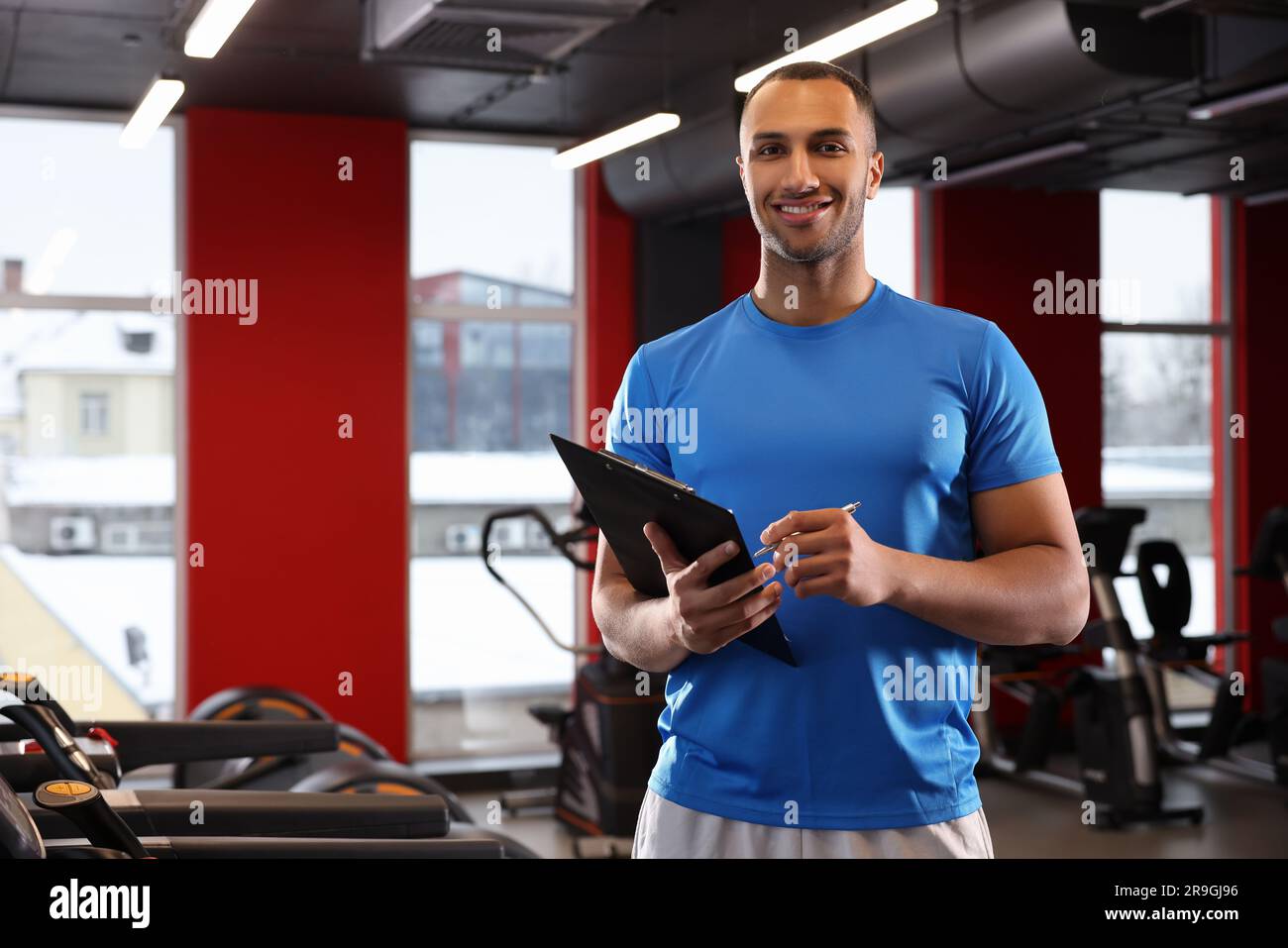 Happy trainer writing down workout plan in modern gym, space for text ...