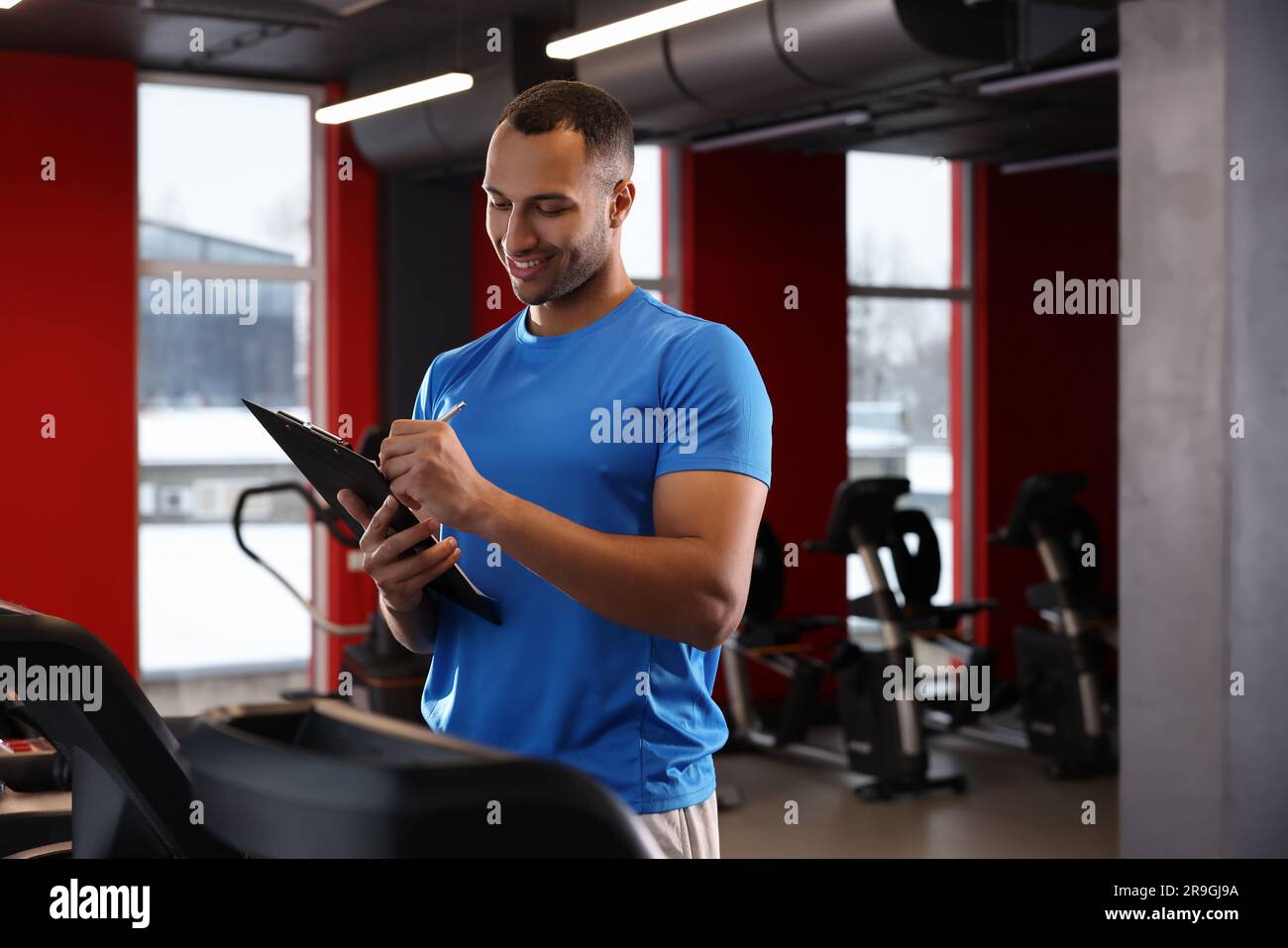 Happy trainer writing down workout plan in modern gym, space for text ...