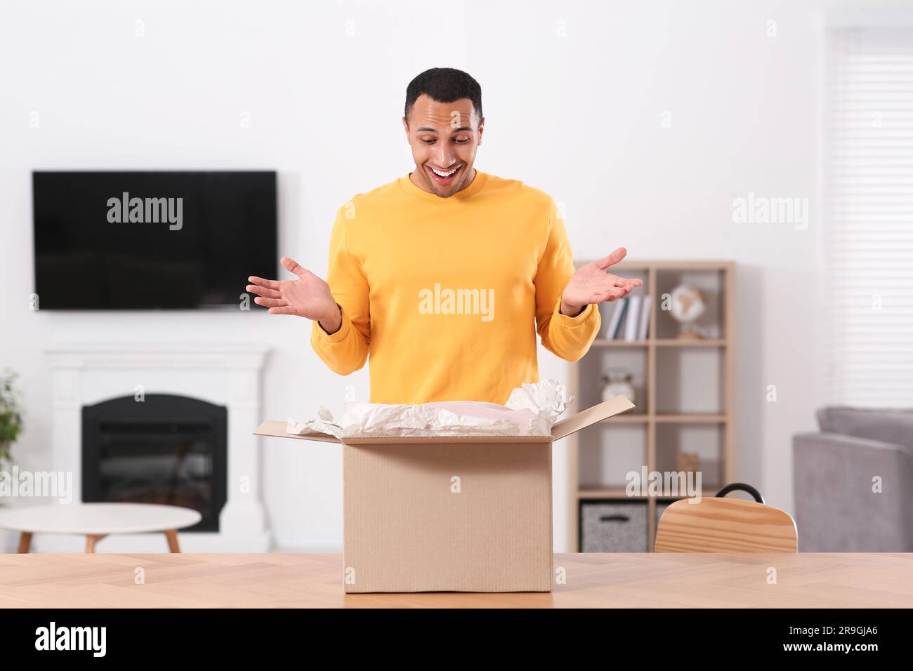 Emotional young man opening parcel at table indoors. Internet shopping ...