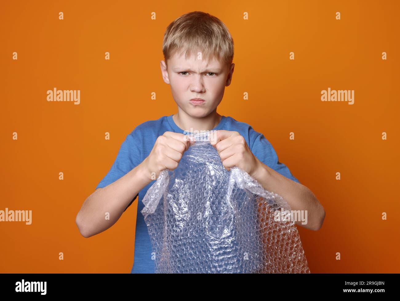 Angry boy popping bubble wrap on orange background. Stress relief Stock ...