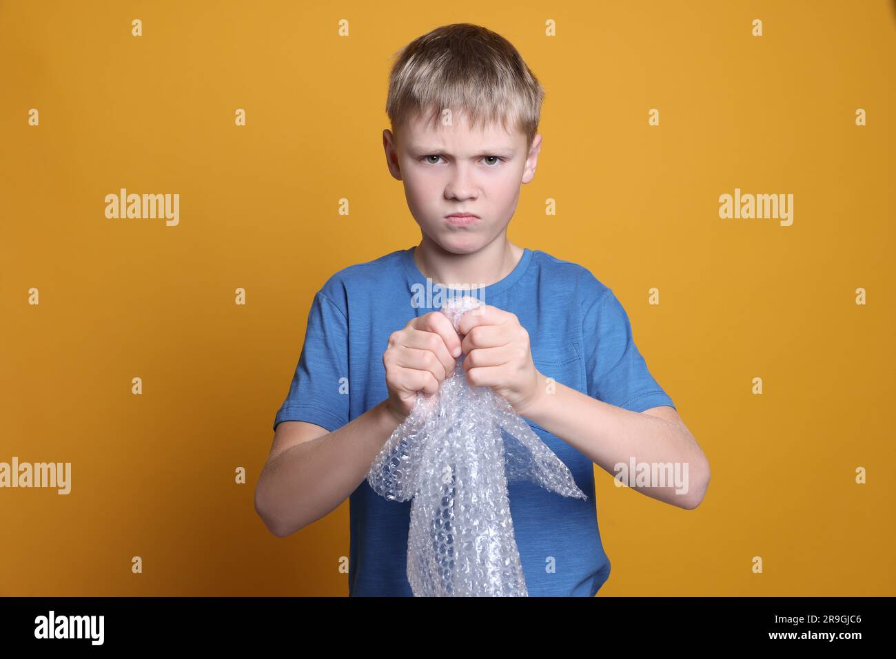 Angry boy popping bubble wrap on yellow background. Stress relief Stock ...