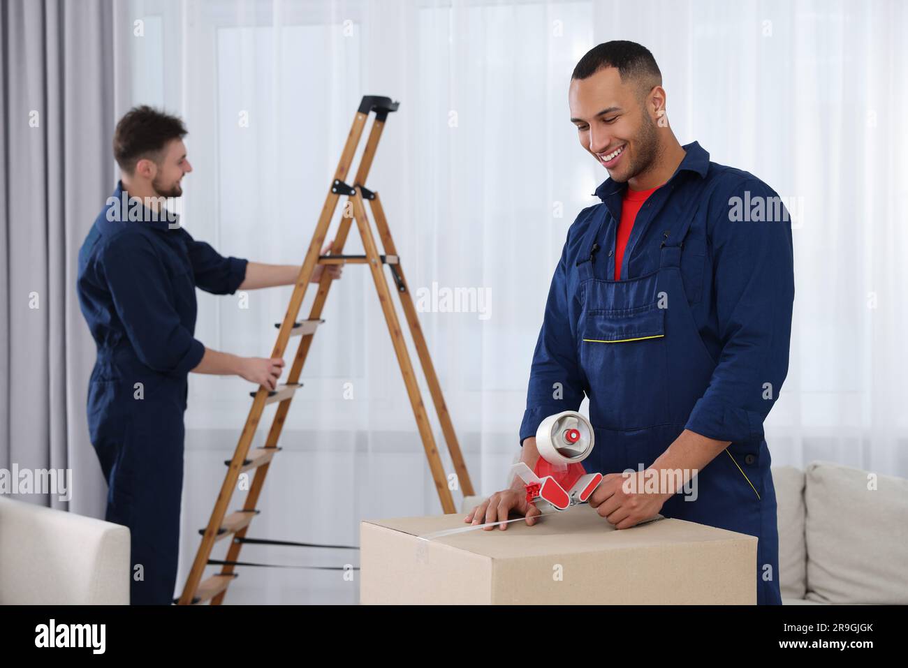 Male mover packing box with adhesive tape in house Stock Photo - Alamy