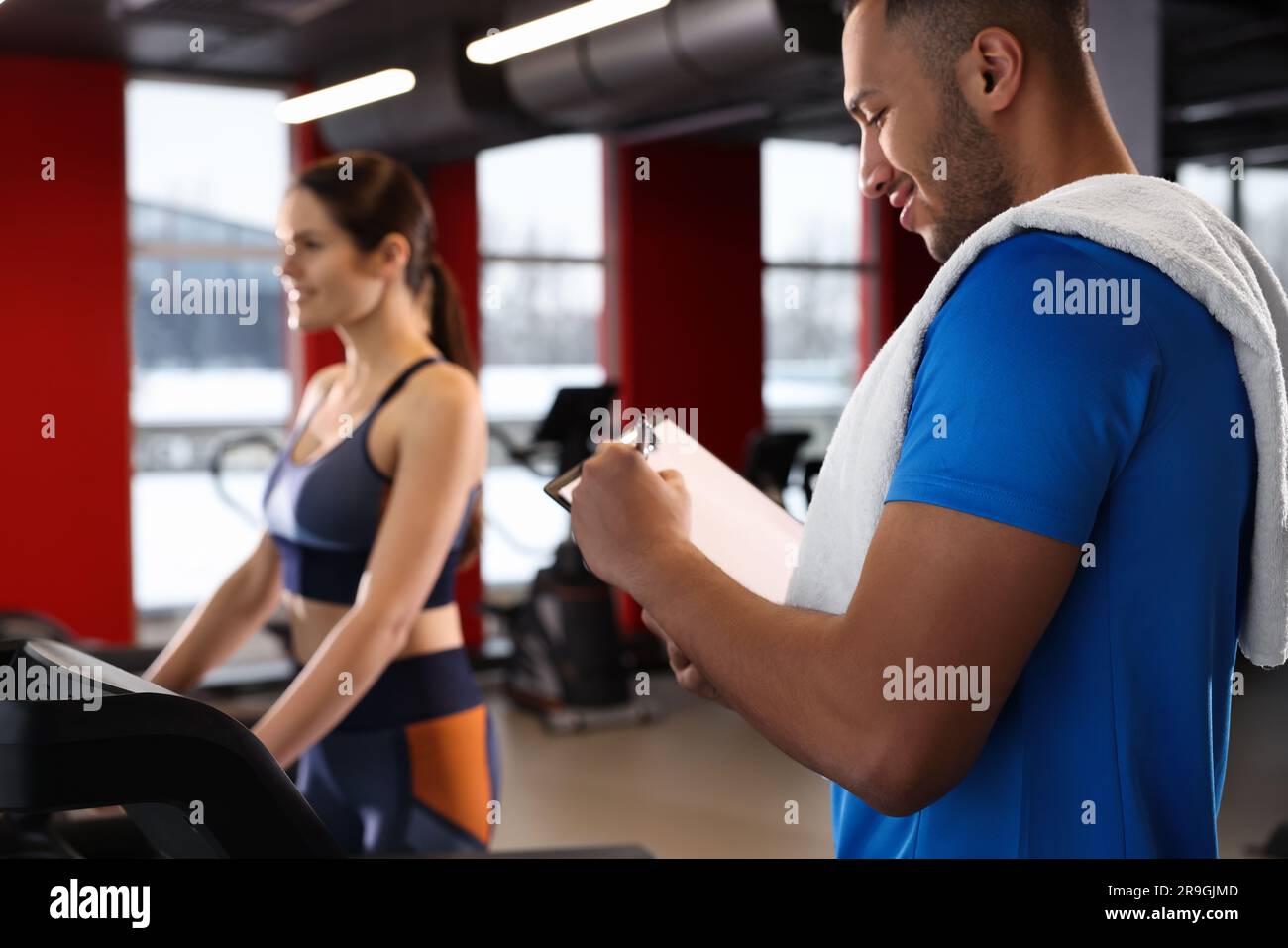 Happy trainer writing down workout plan while woman doing exercise in ...
