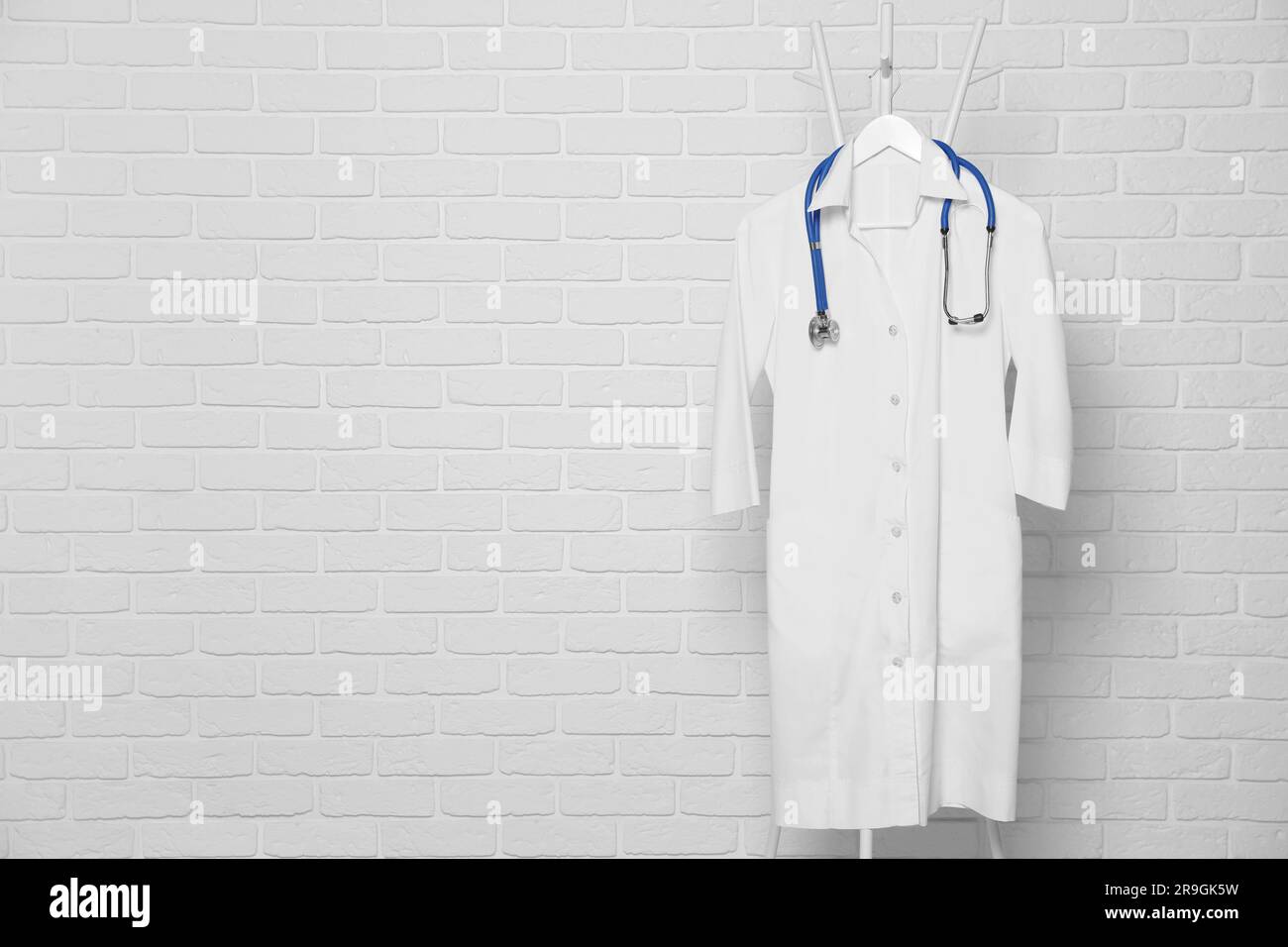 Medical uniform and stethoscope hanging on rack near white brick wall ...