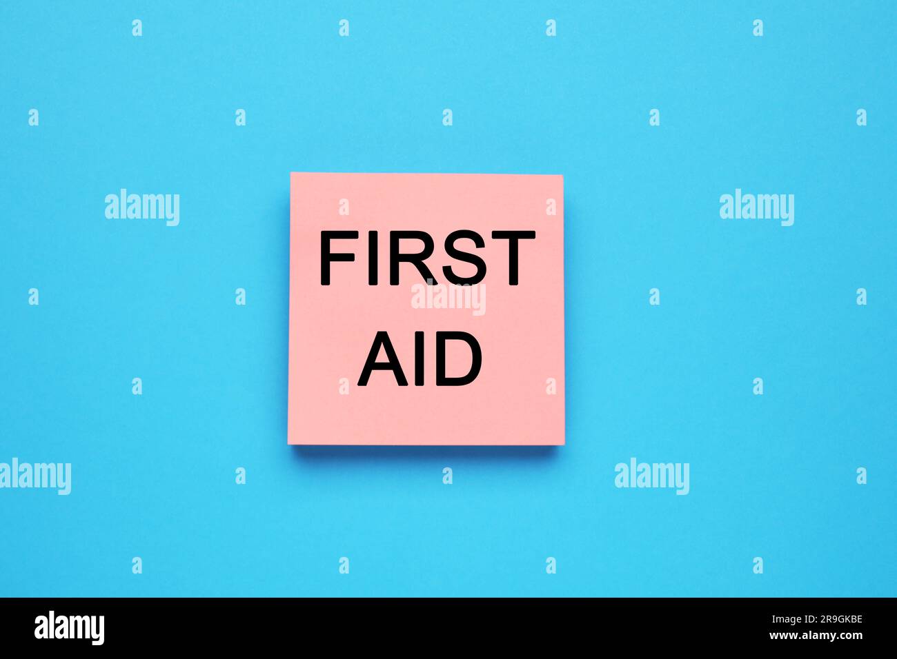 Pink paper note with words First Aid on light blue background, top view ...