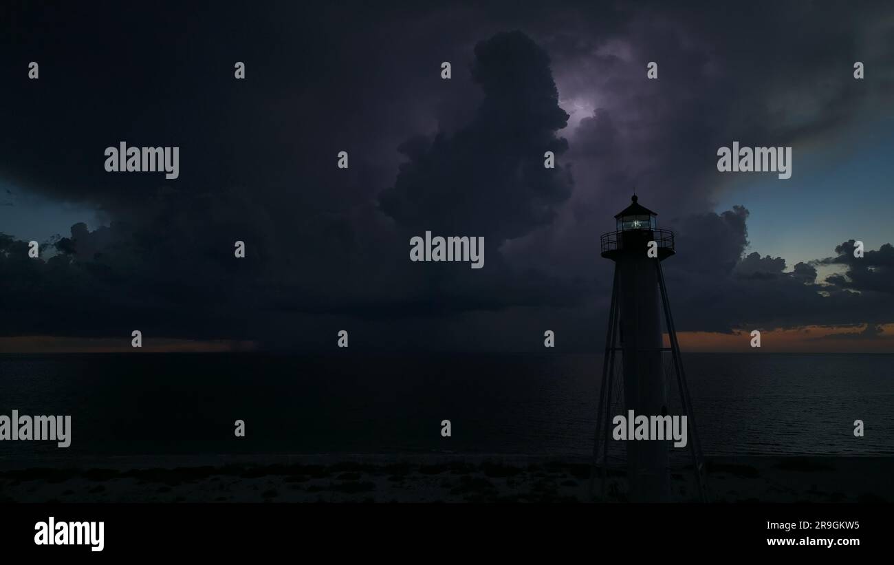 White tall lighthouse on sea shore with blinking light at stormy night ...