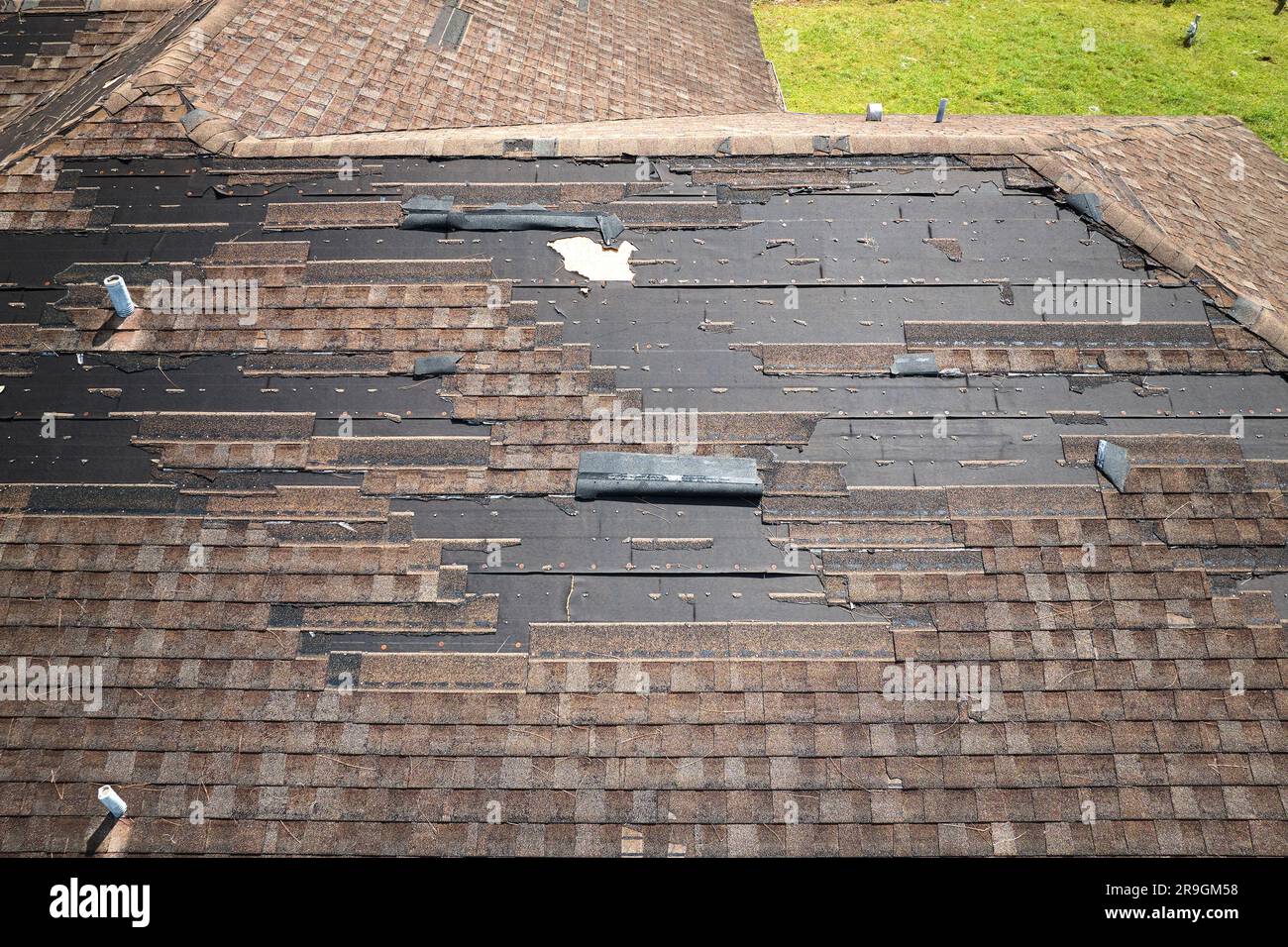Wind damaged house roof with missing asphalt shingles after hurricane ...