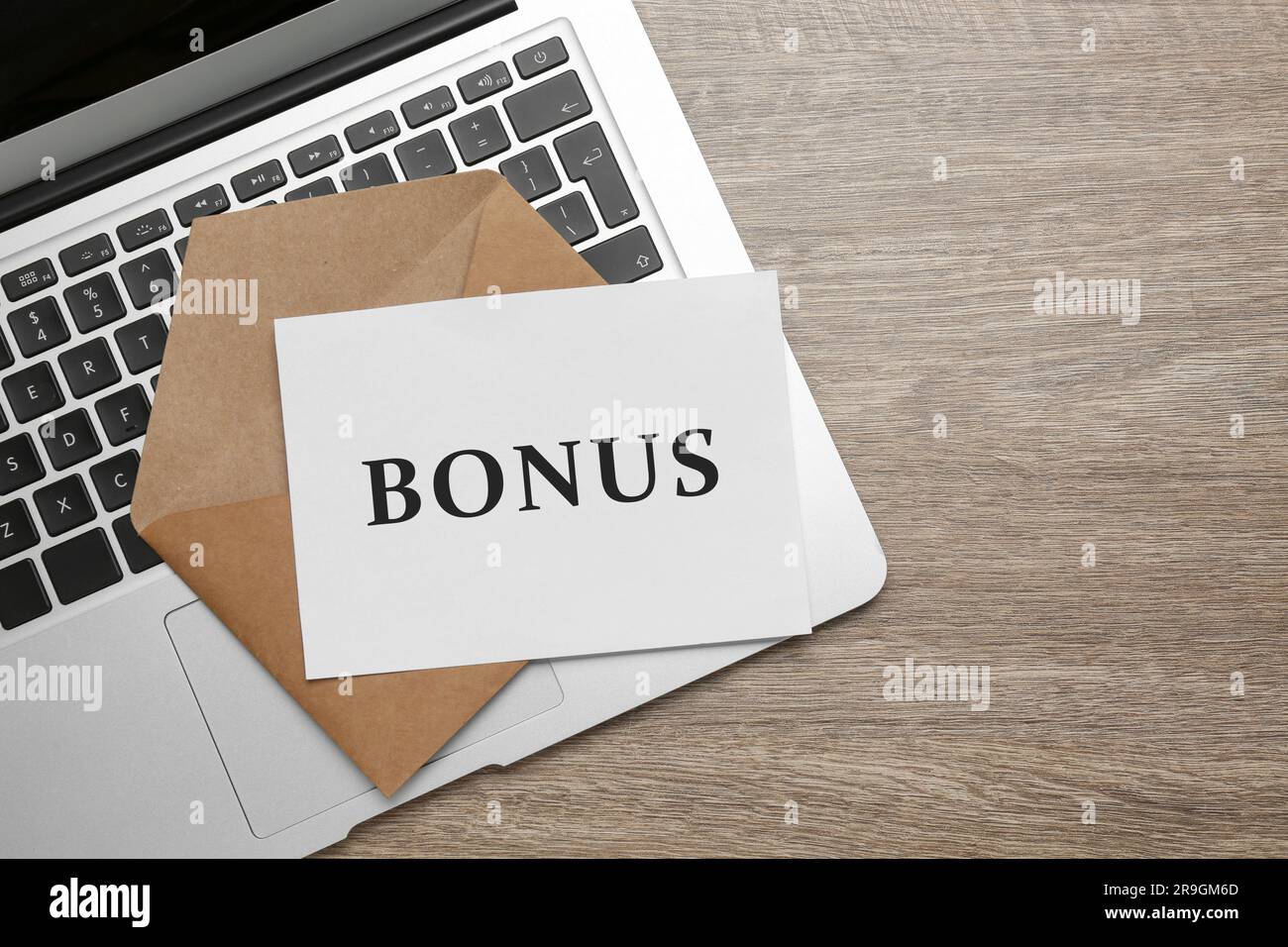 Brown envelope, letter with word Bonus and laptop on wooden table, top ...