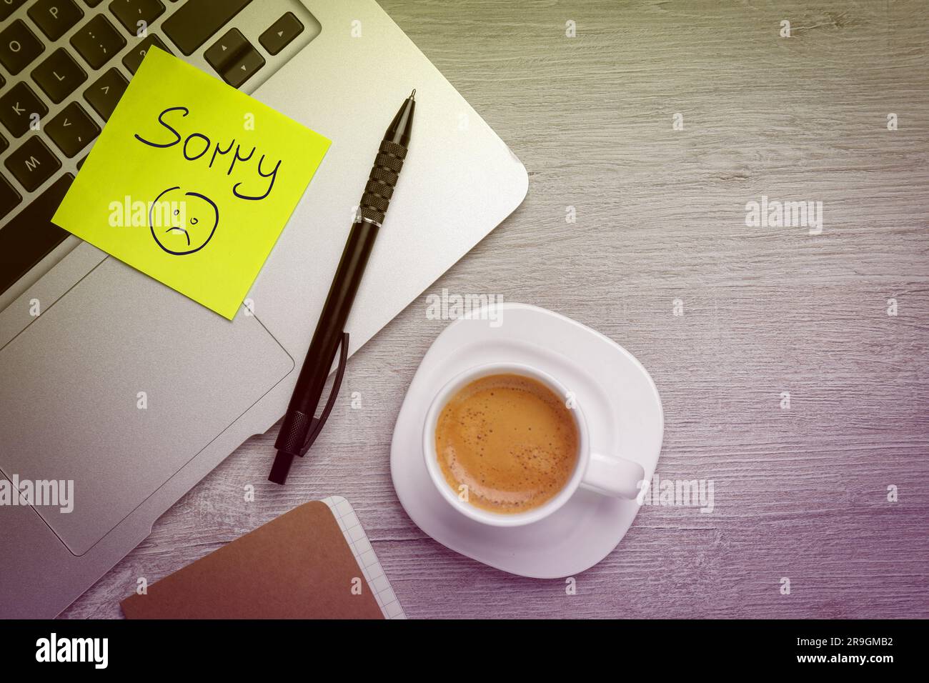 Sticky note with word Sorry and drawn sad face attached to laptop on ...