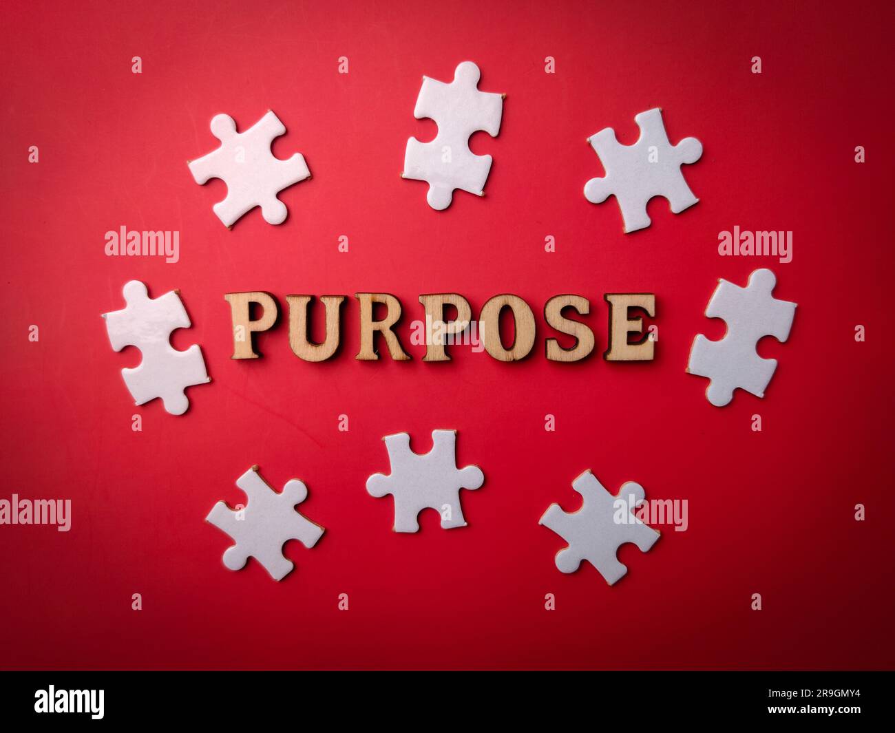 Top view wooden word and white puzzle with the word PURPOSE on a red ...