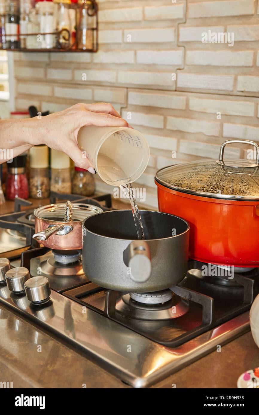 Chef pours water from a measuring cup into pot on gas stove Stock Photo ...