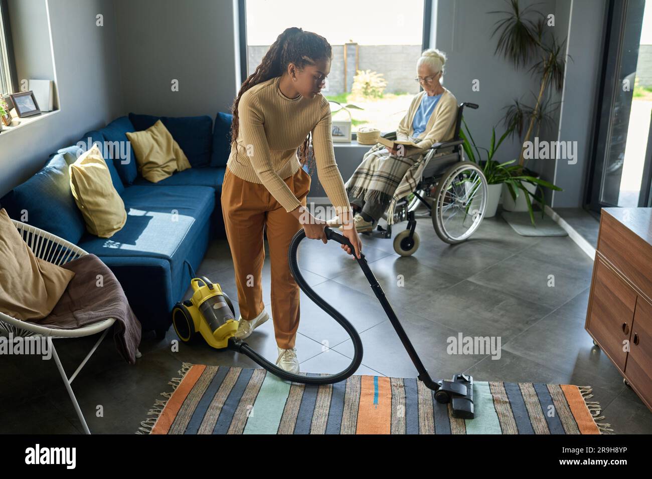 Youthful girl with vacuum cleaner helping her grandmother with ...