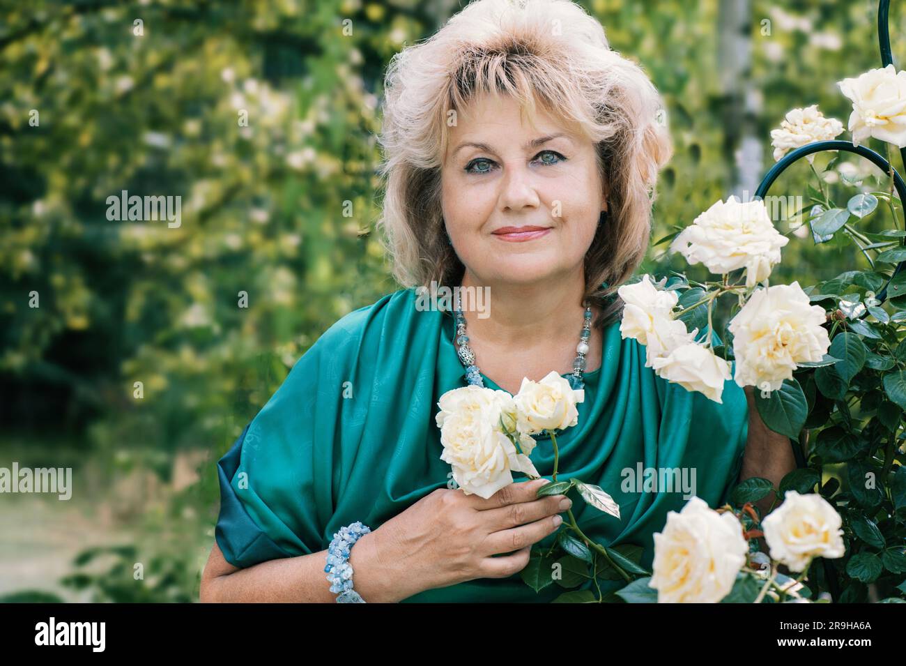 59-year-old woman in the garden. A mature woman enjoys the flowers of a ...