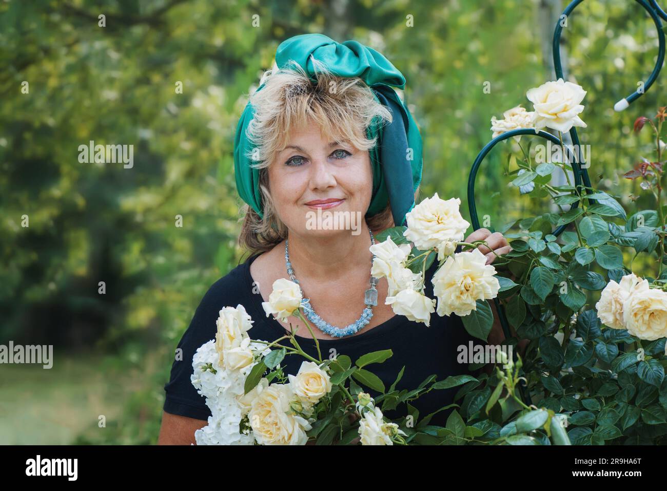 59-year-old woman in the garden. A mature woman enjoys the flowers of a ...