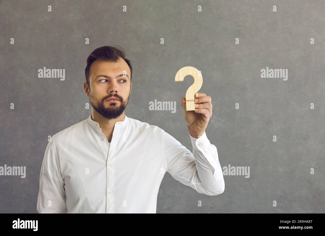 Puzzled young man holding a question mark and thinking of an answer to ...