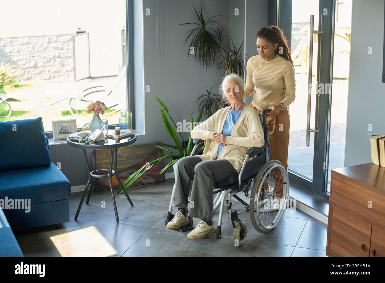 Teenage girl looking at her grandmother in wheelchair and pushing it ...
