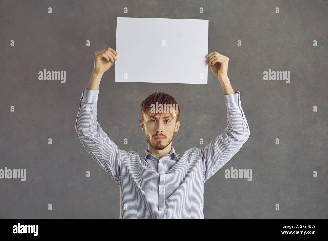 Serious man holding blank white sheet of paper over his head while ...