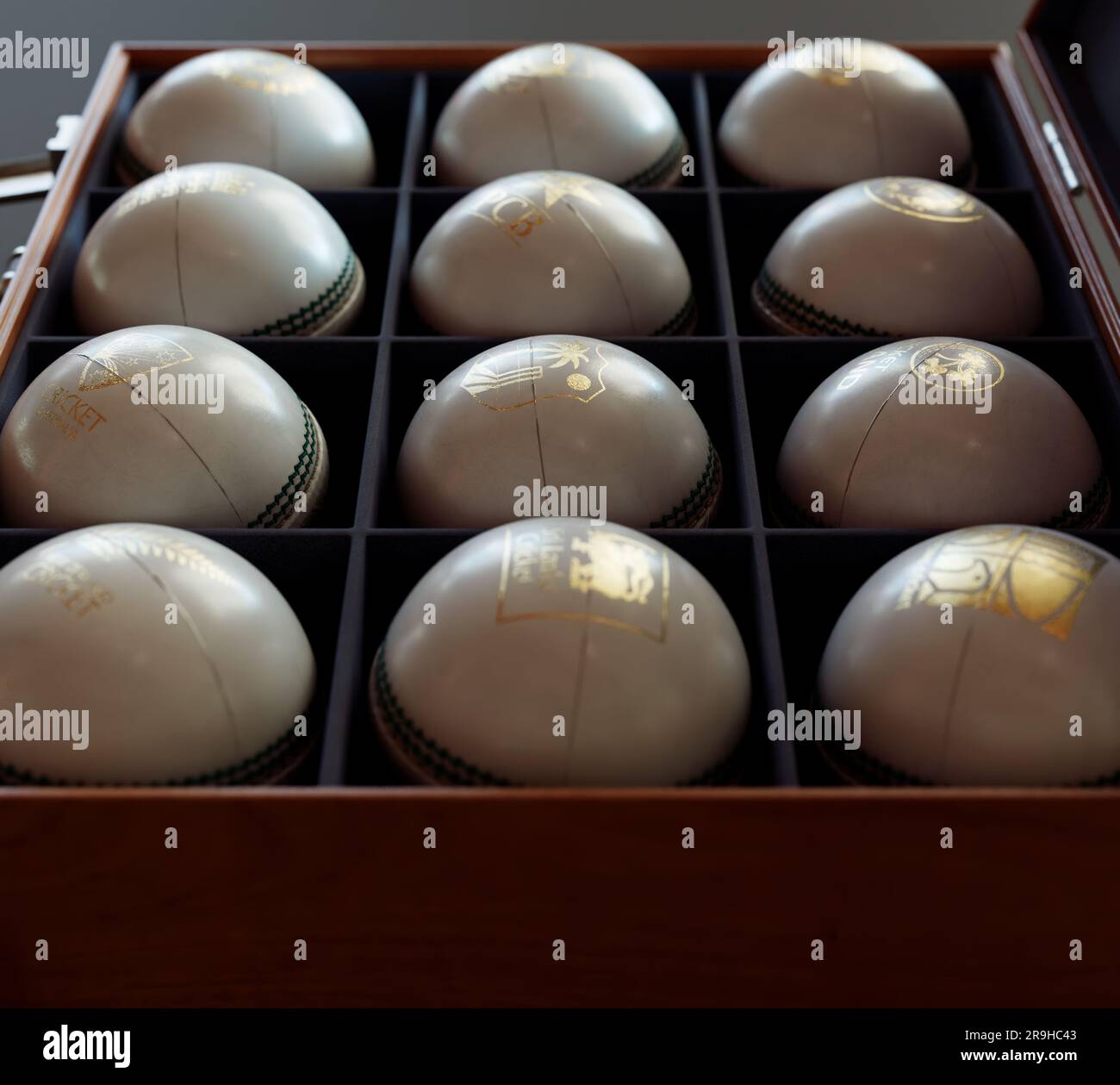 A collection of white cricket balls imprinted with gold logos of the ...