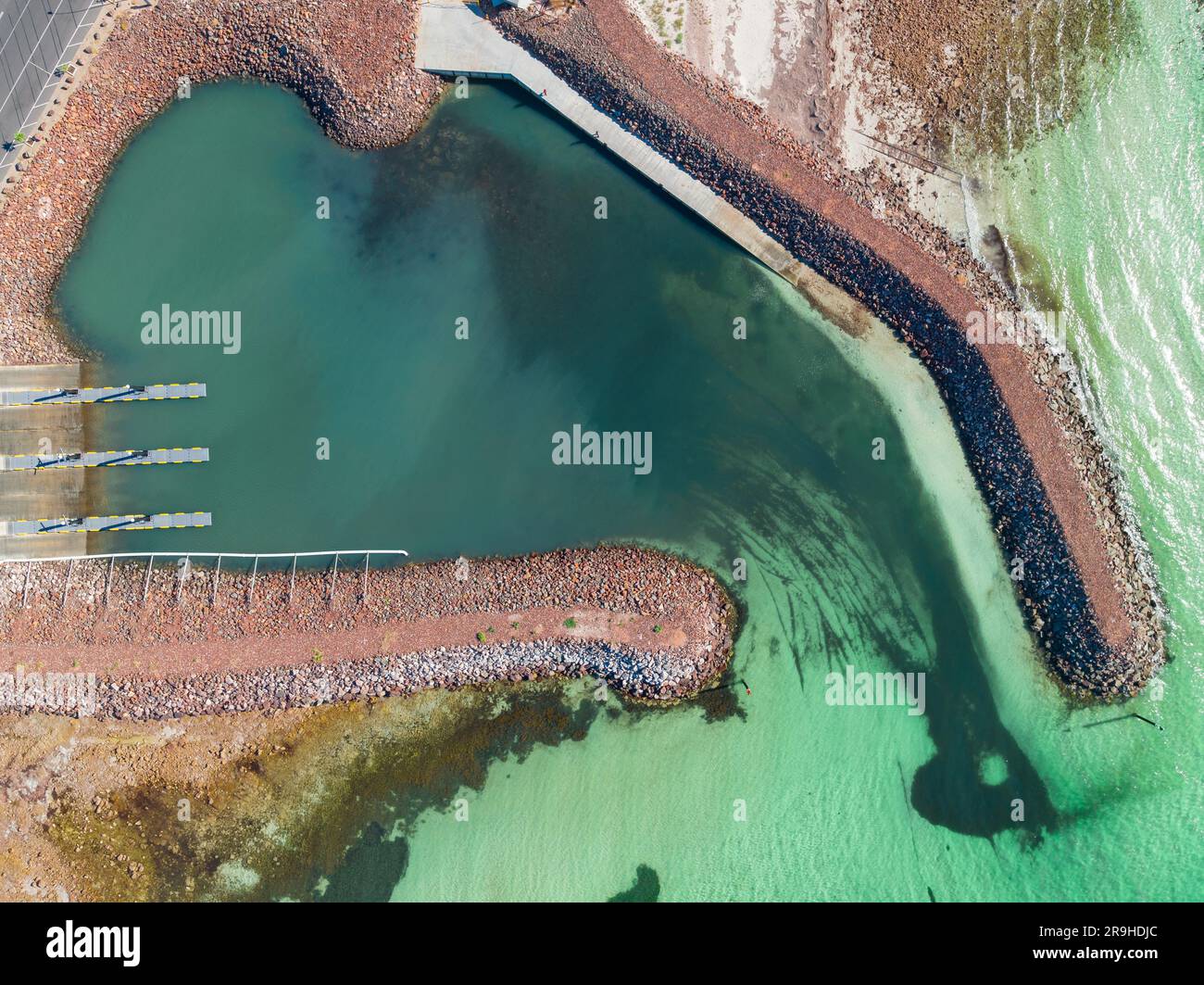 Aerial view of a coastal boat ramp surrounded by rocky breakwaters at ...