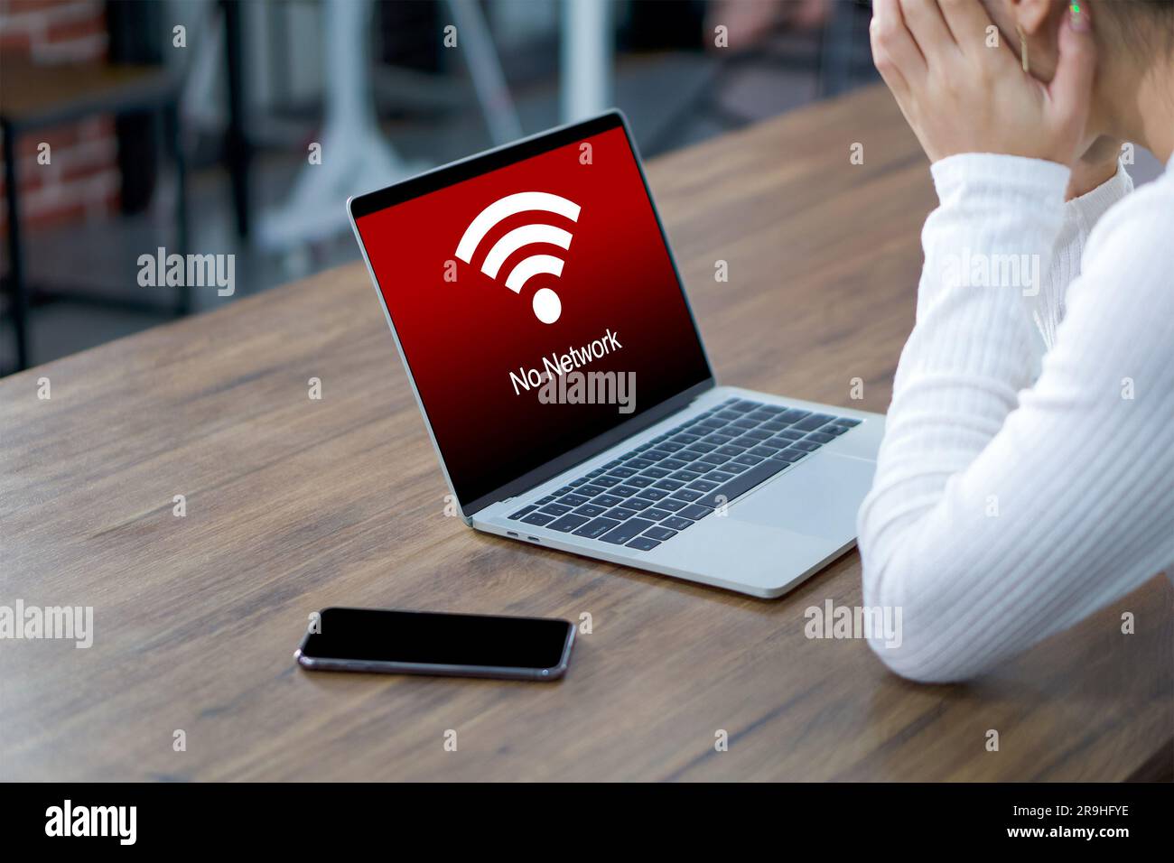 Woman holds her temple with both hands, sitting in front of laptop ...