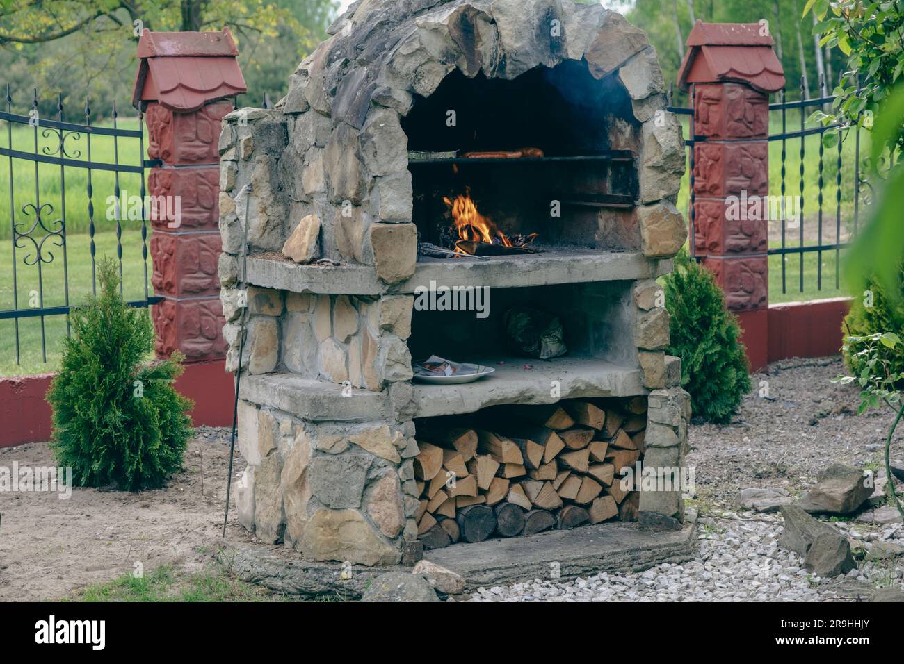 Stone barbecue in the garden with fire - fence and plants in the ...
