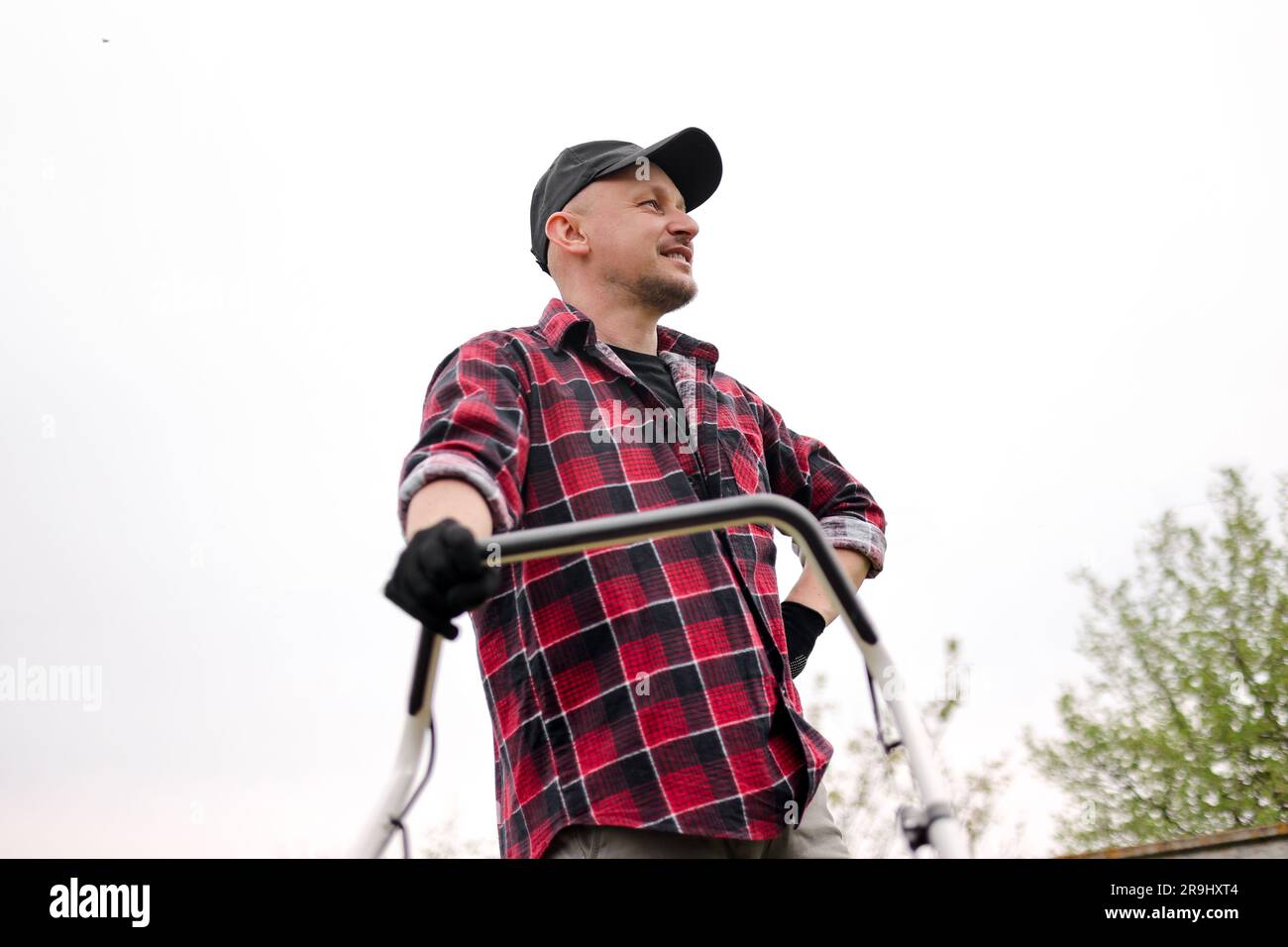Bottom view of tired man makes a short break while cutting grass with a ...