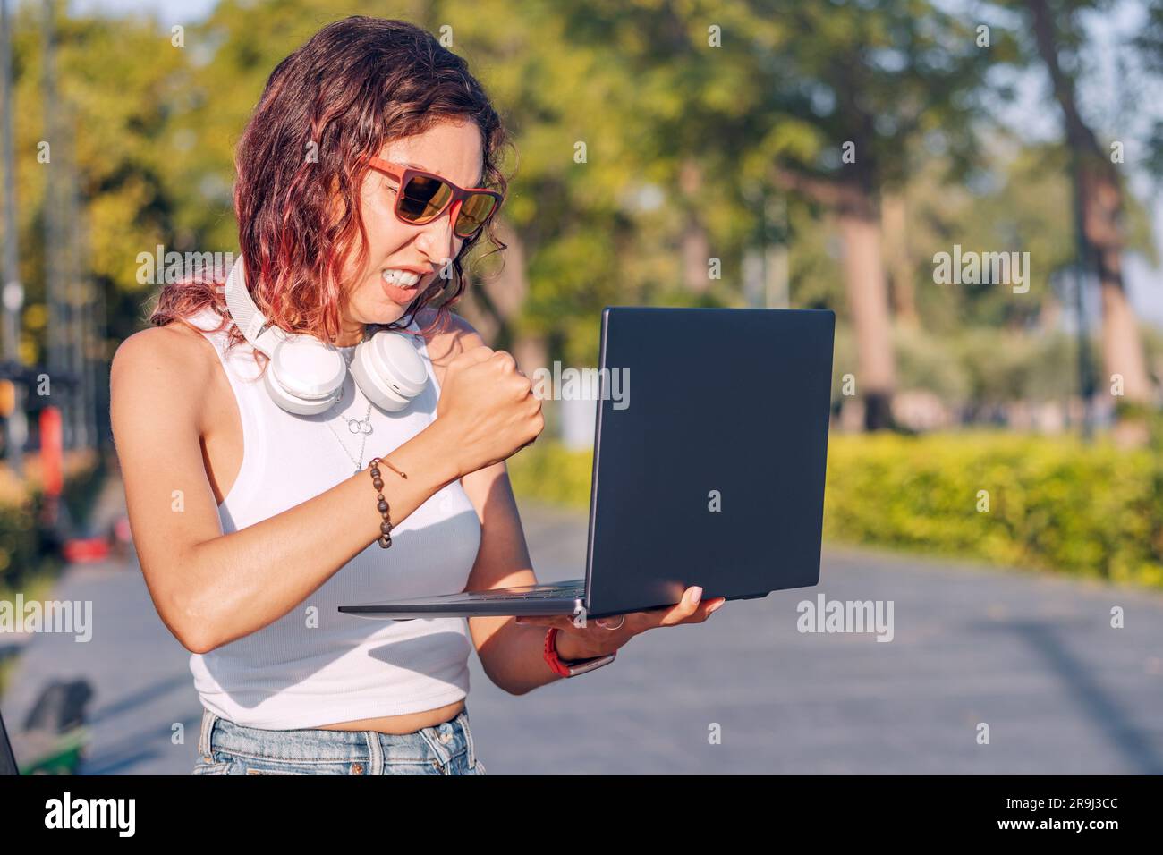 An angry and annoyed woman swears and raises her fist at her laptop ...
