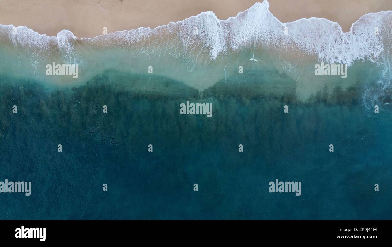 An aerial view of sea waves crashing against a beach in the daylight ...