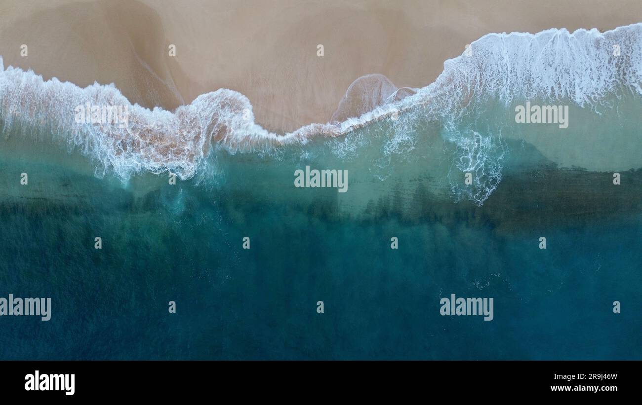 An aerial view of sea waves crashing against a beach in the daylight ...