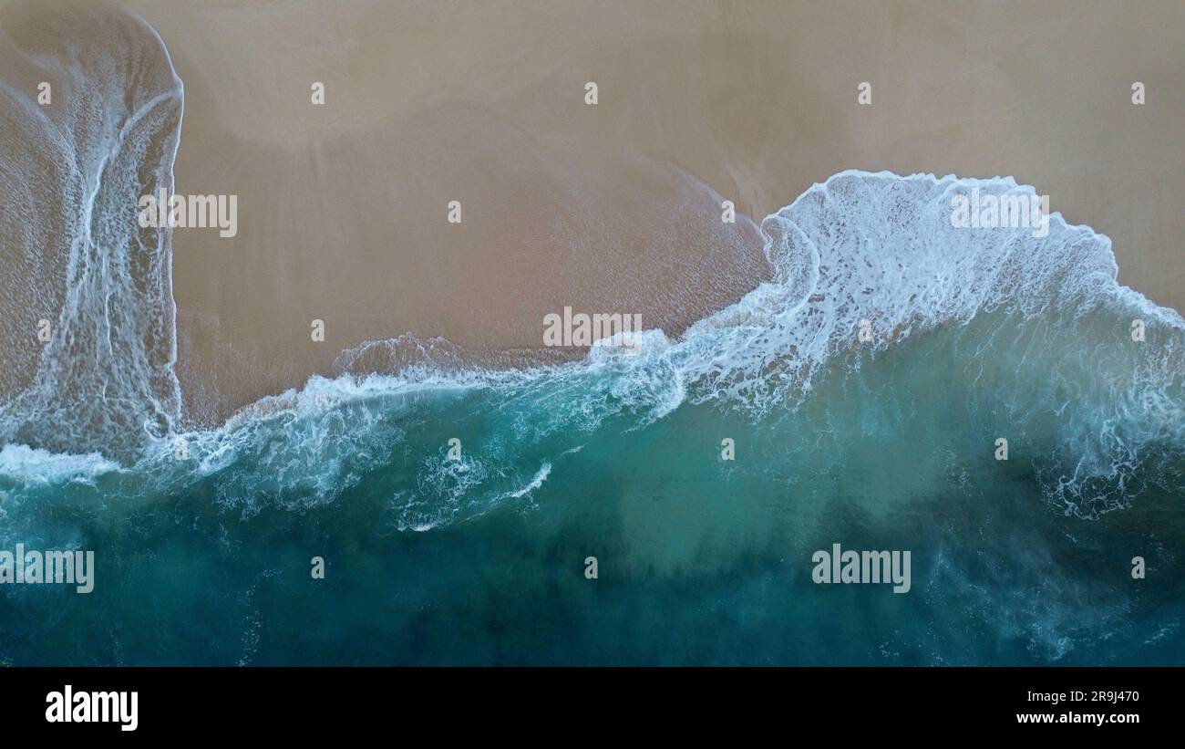 An aerial view of sea waves crashing against a beach in the daylight ...