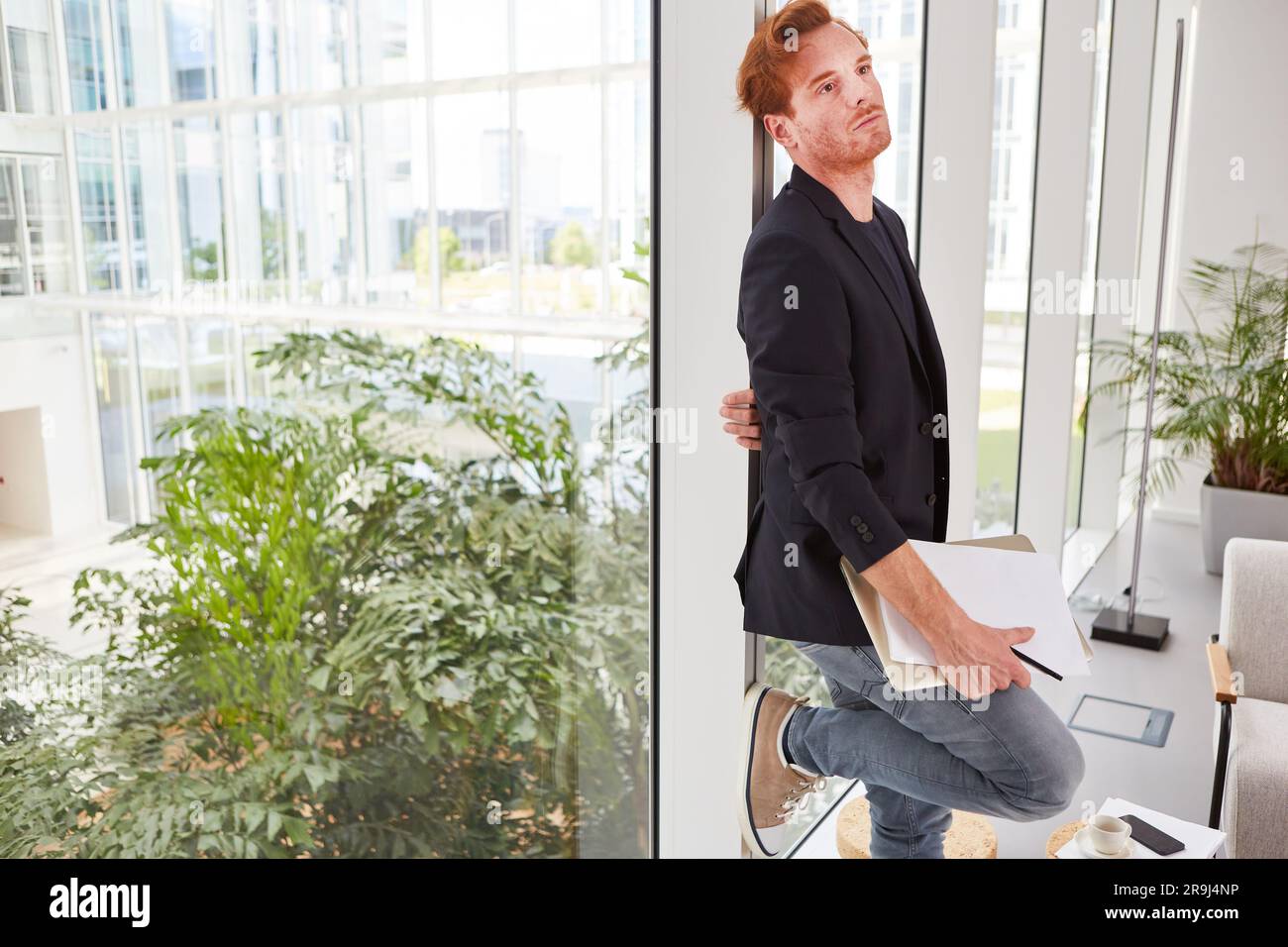 Thoughtful female professional leaning on window in lounge Stock Photo ...