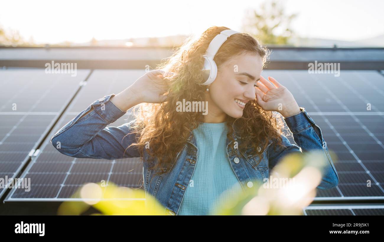 Portrait of young excited woman on roof with solar panels, listening ...