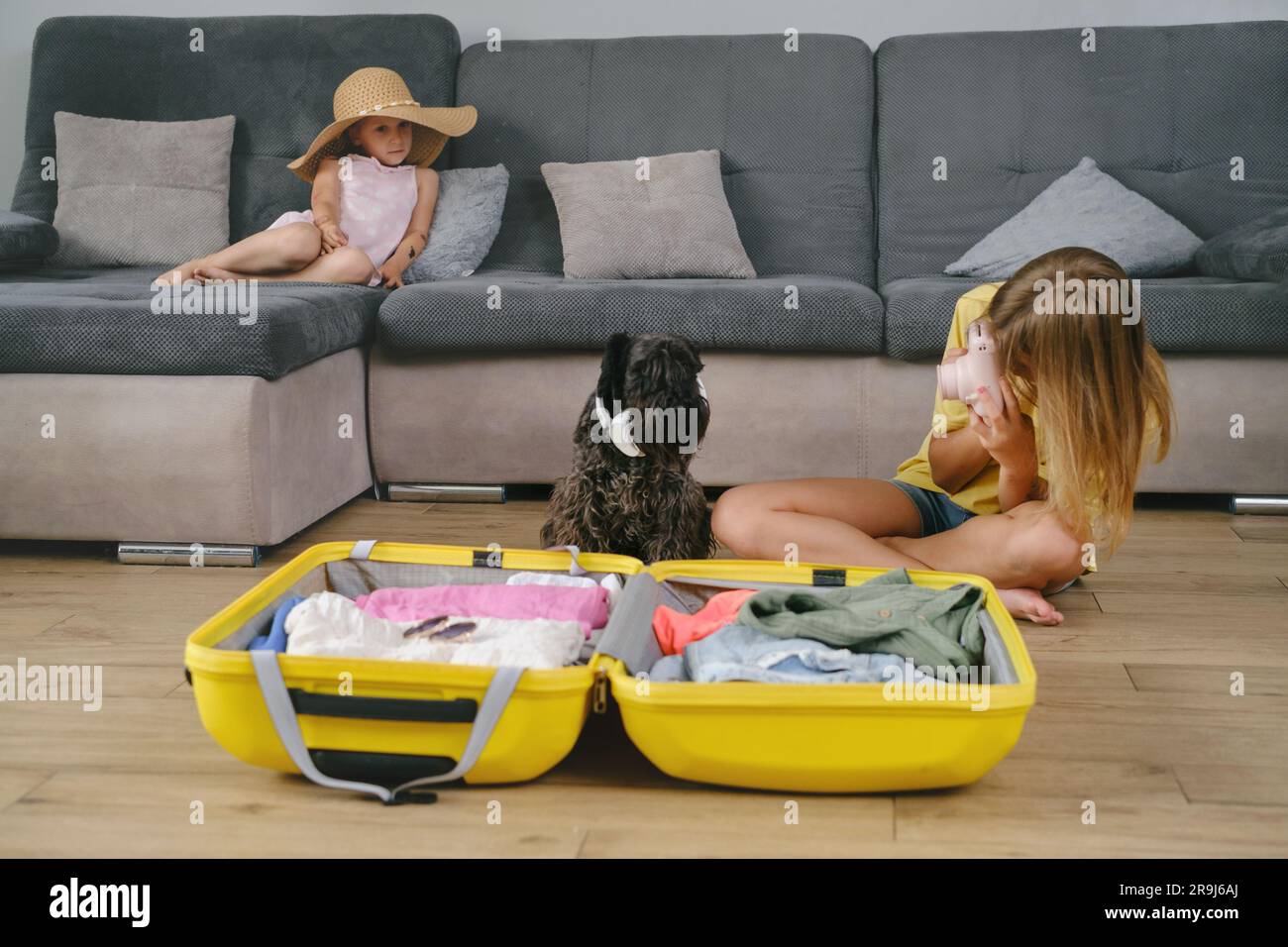 Children packing suitcase for travel and play with a dog. Sisters having fun with pet while ...