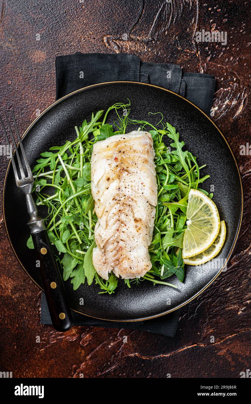 Grilled cod fish fillet served with green salad in a plate. Dark ...