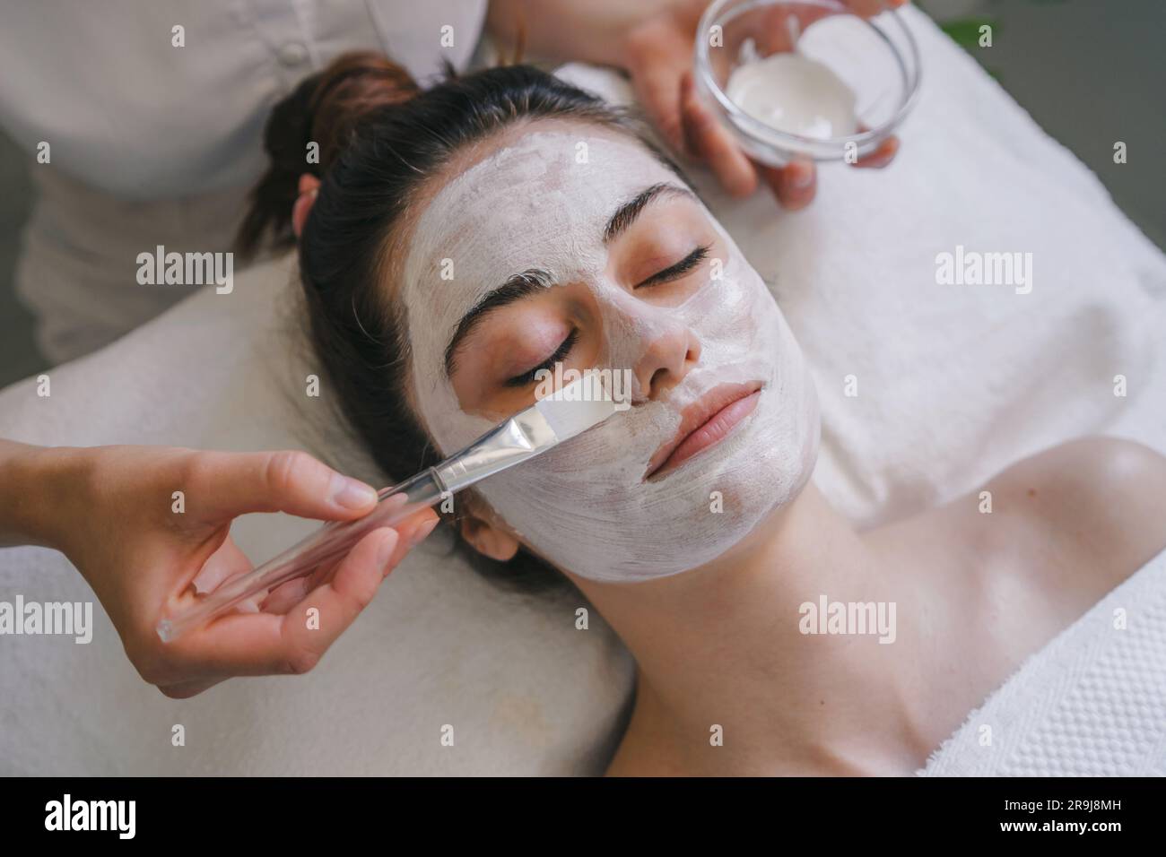Top view of crop anonymous female applying facial mask on face while ...