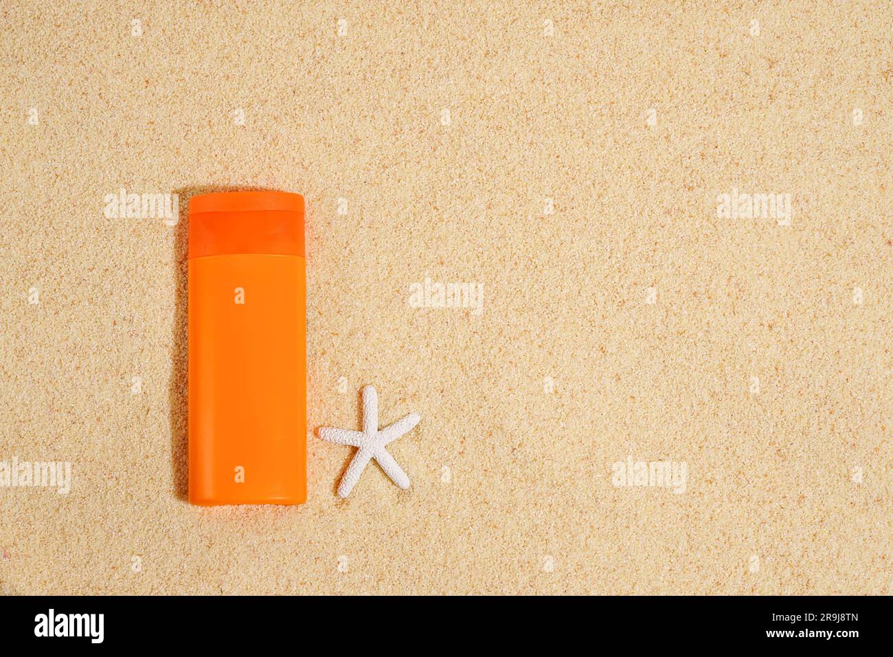 Sunscreen in orange plastic tube with white starfish on sand background ...