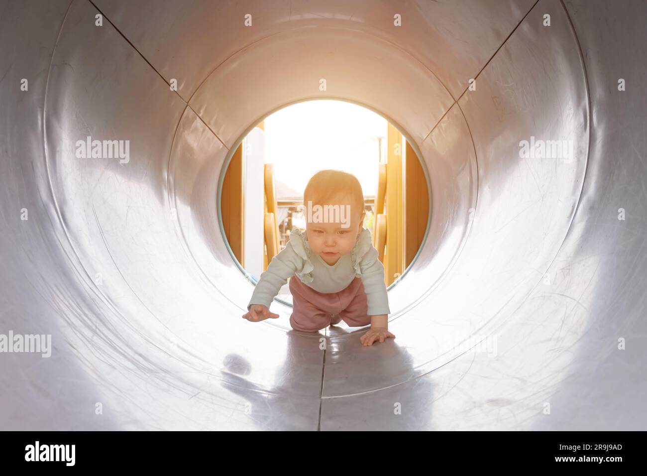Toddler girl likes to crawl along gray pipe on playground Stock Photo ...
