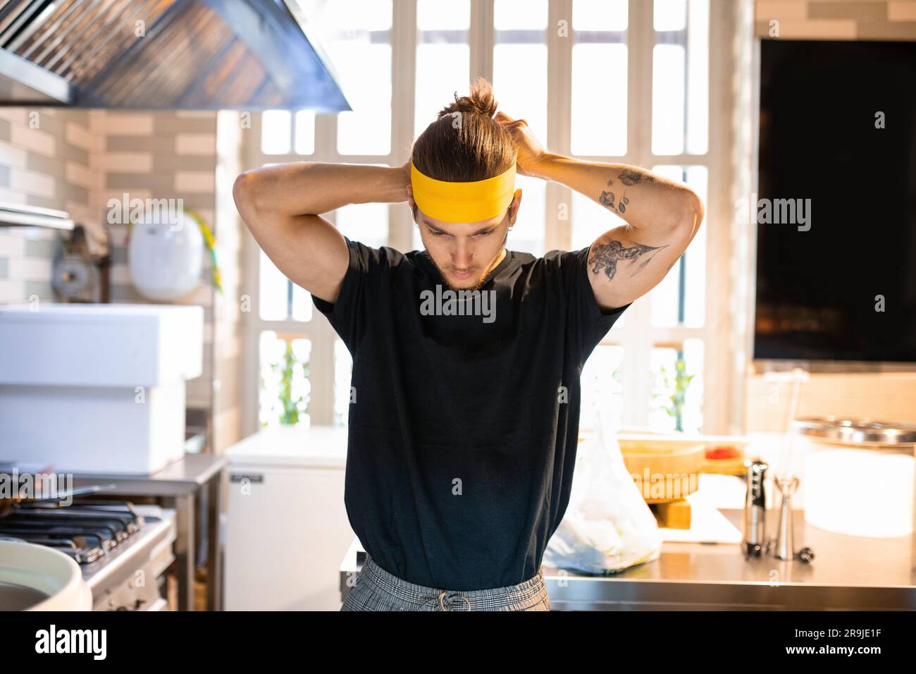 Concentrated young male cook tying yellow band around head and looking ...