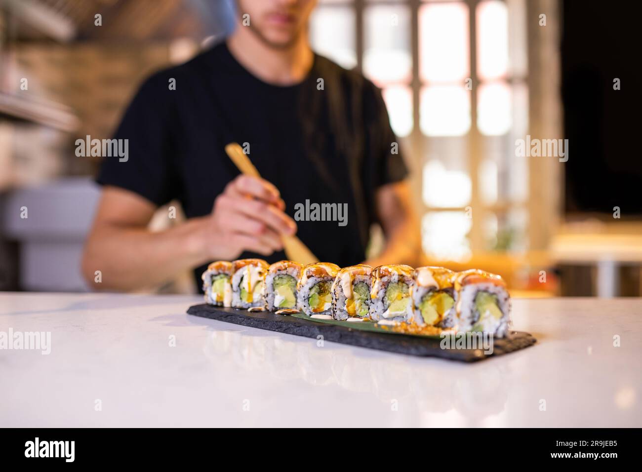 Anonymous young man with sitting at kitchen table with maki sushi rolls ...