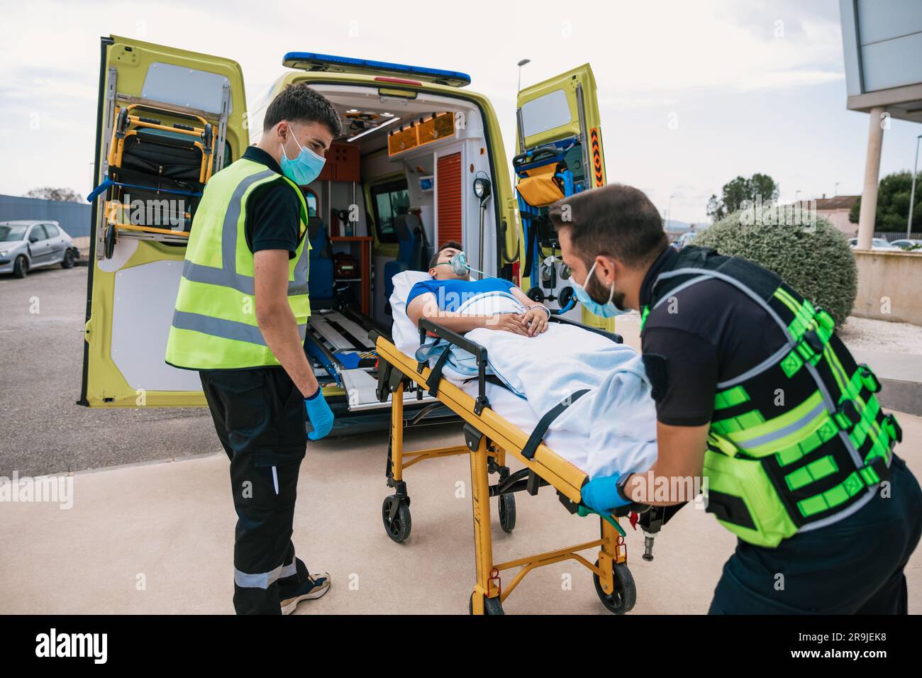 Paramedics in uniform and medical masks loading patient on stretcher ...