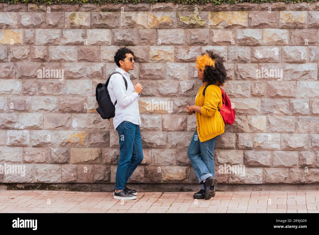 Side view of young friends in casual clothes with backpacks facing each ...