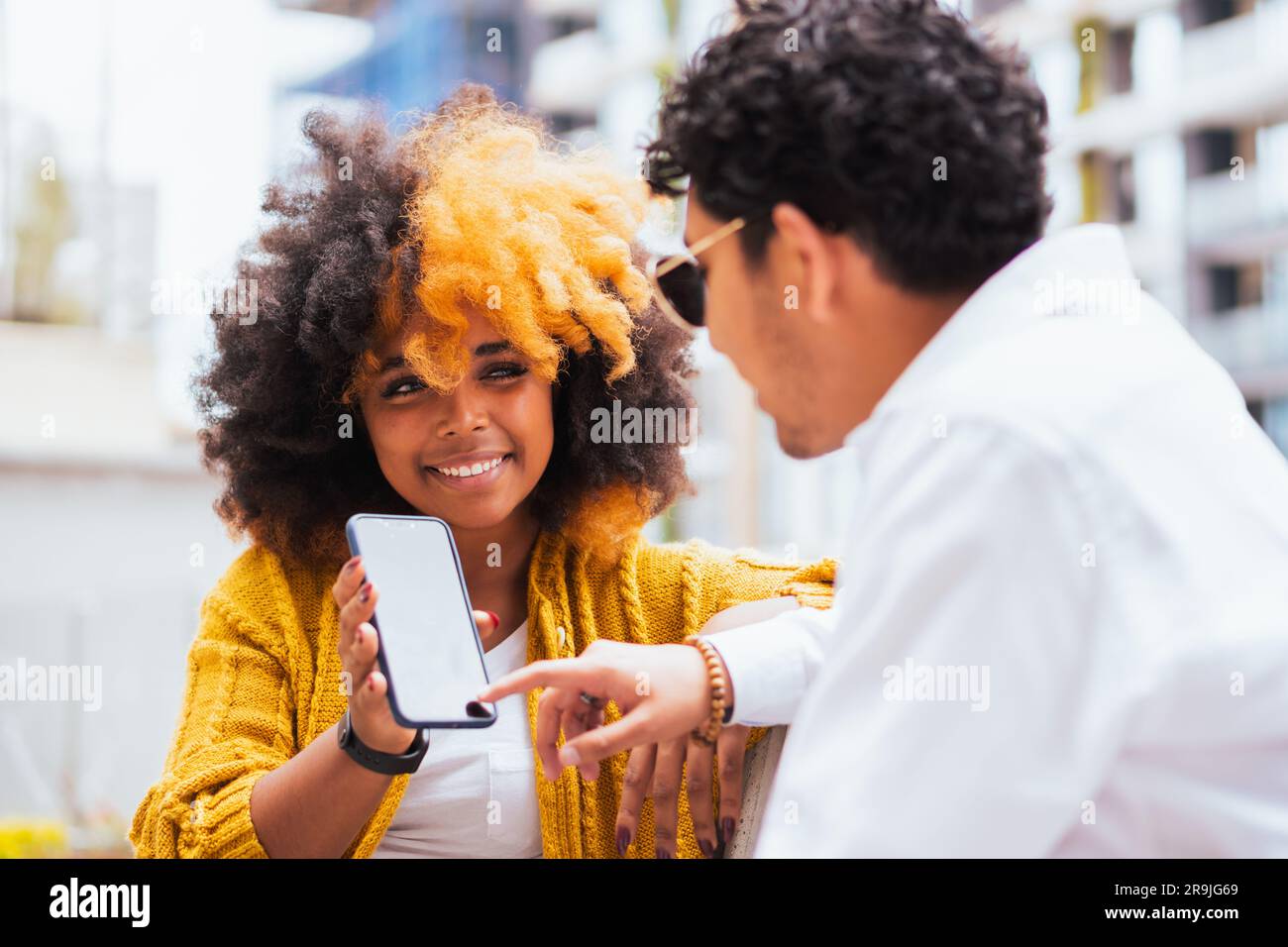 Happy black female with Afro yellow hair in casual clothes smiling and looking at male anonymous ...