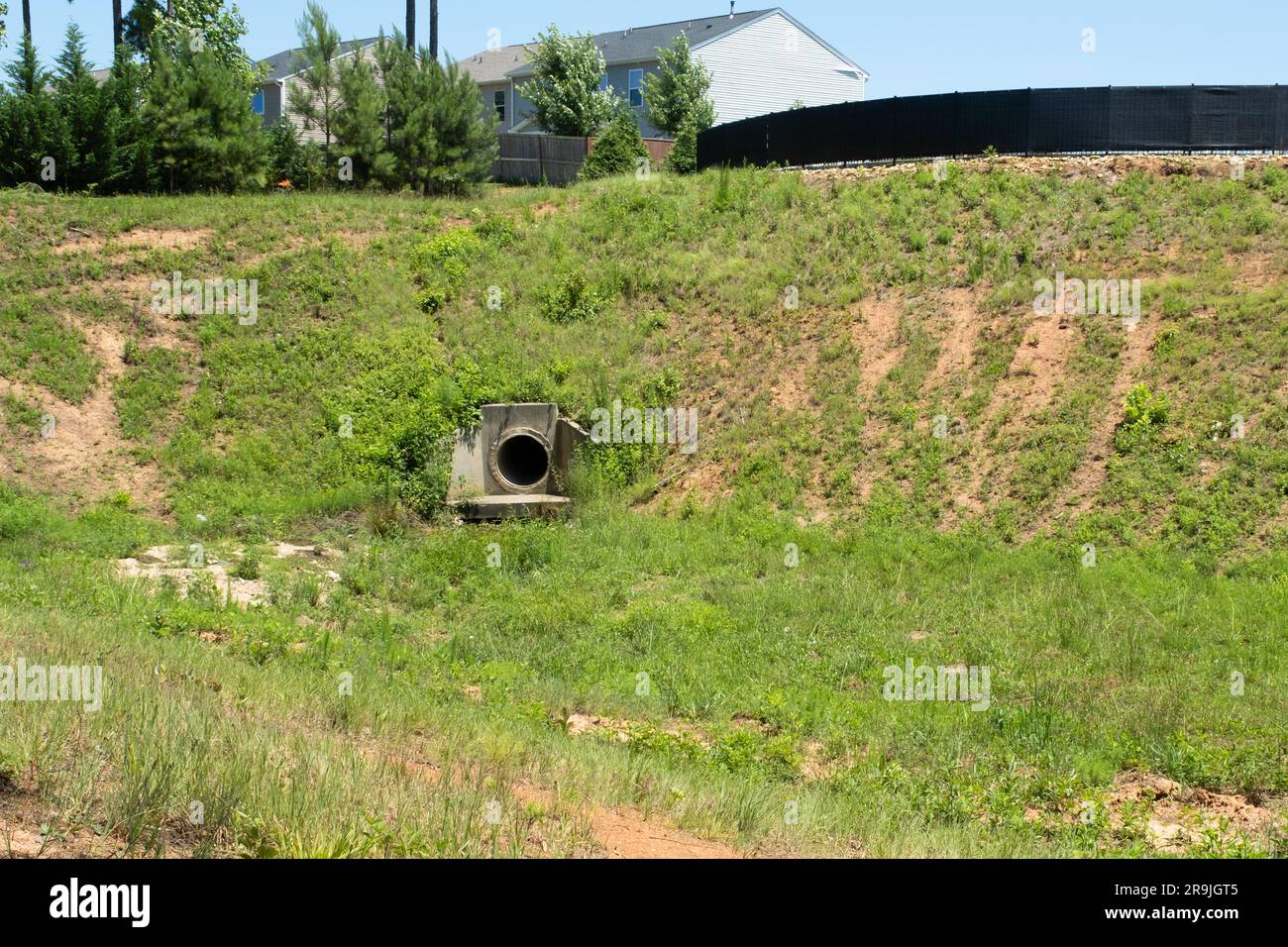 Large drainage ditch lined with grass and weeds behind a subdivision ...