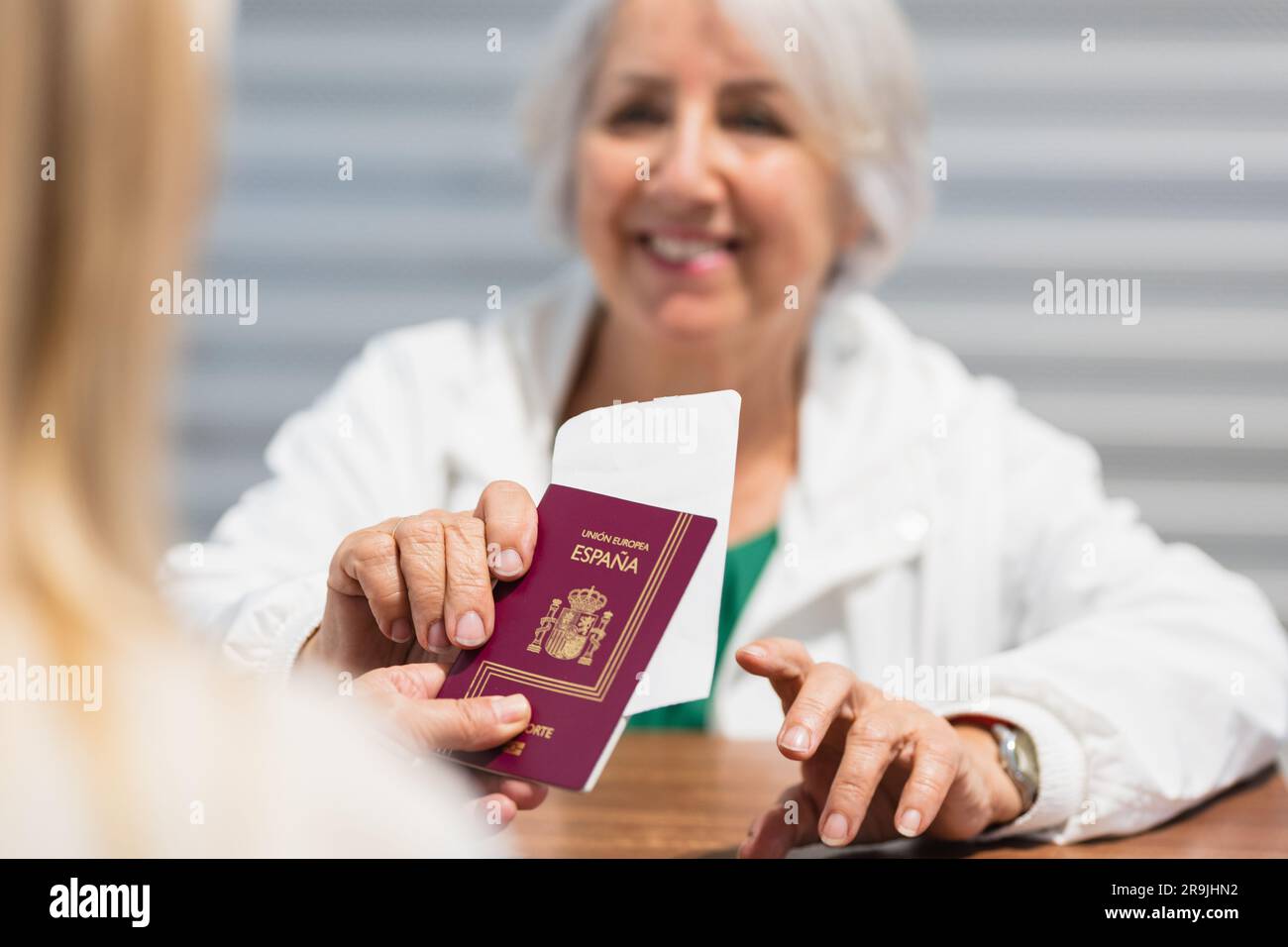 Crop smiling elderly lady in white jacket receiving passport from ...