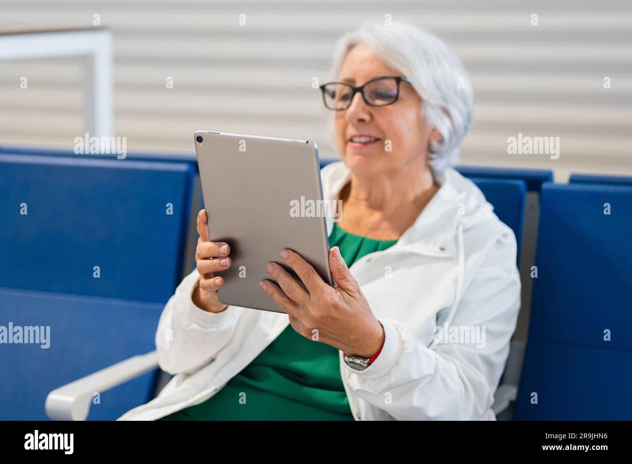 Positive elderly female with short gray hair watching film on tablet ...