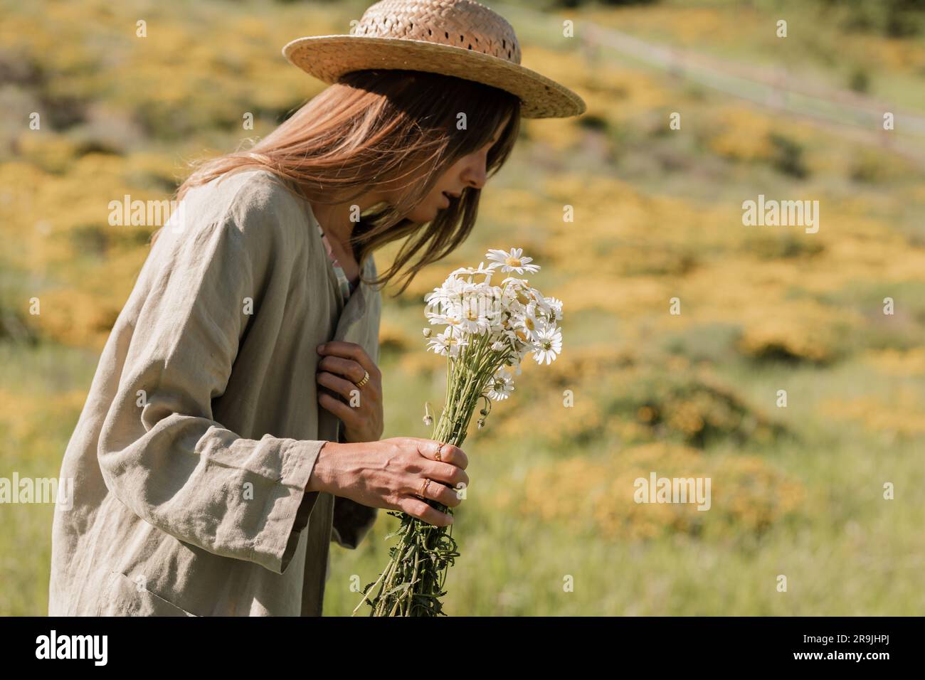 Side view of female in casual wear and hat holding bouquet of daisies ...