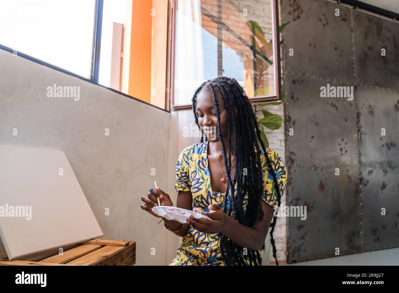 Happy female painter with long deadlocks holding palette while painting ...