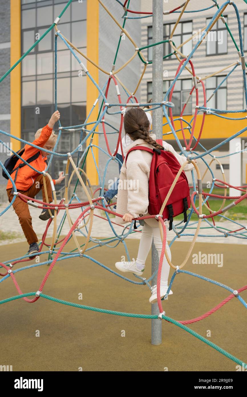 Full body of children in casual clothes with backpack climbing network ...