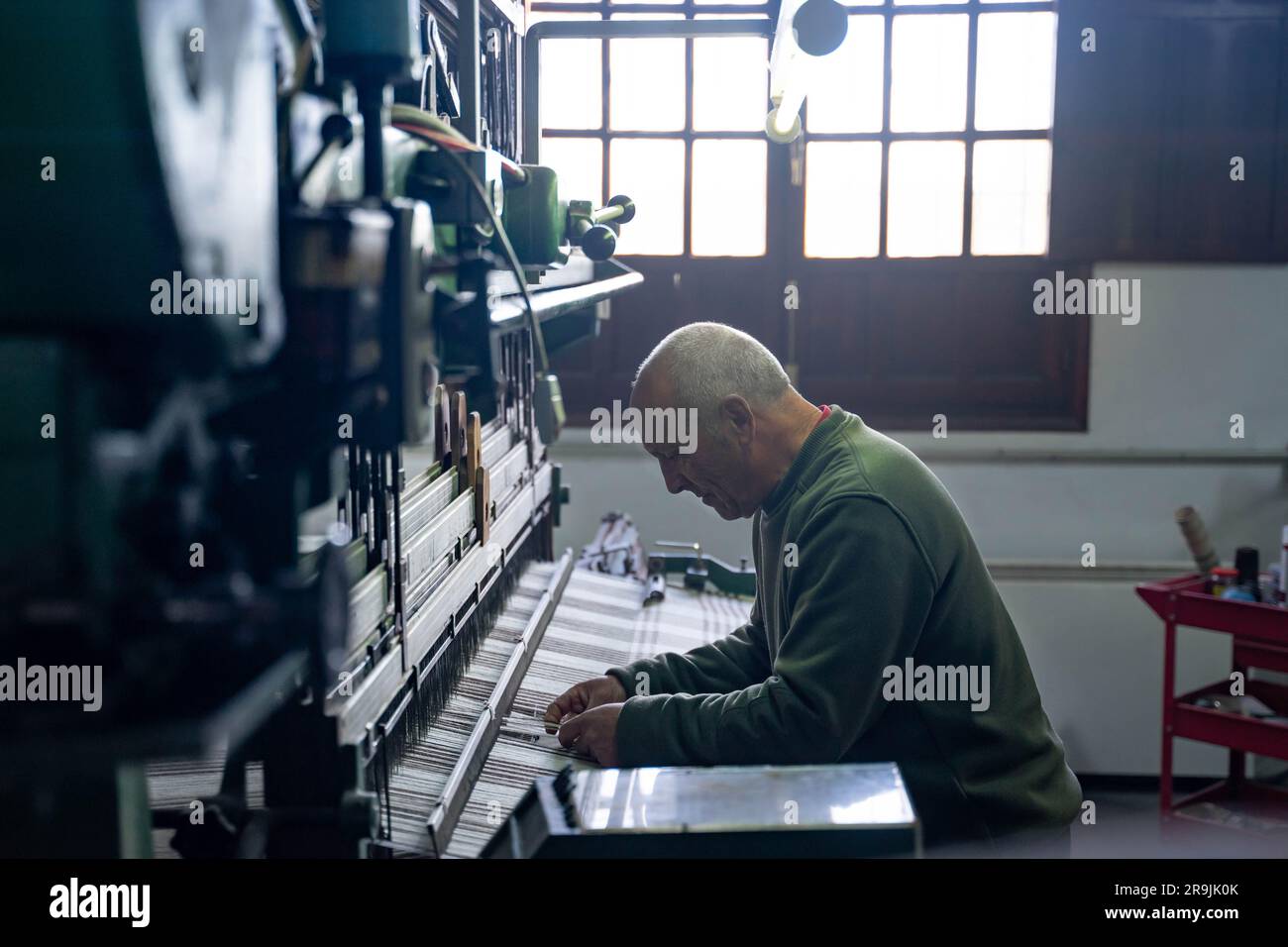 Side view of concentrated senior male worker sitting at workbench and ...